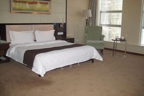 Quarto de hotel com uma cama grande, uma cadeira, uma mesinha e uma janela.
