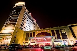 Hotel com fachada curva imponente, ampla entrada com placa e vários carros estacionados no estacionamento.