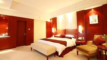 Quarto de hotel com cama grande, mesa de cabeceira, cadeira e escrivaninha com abajur.
