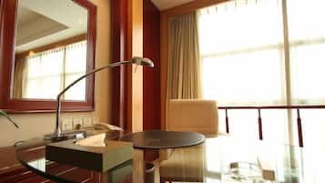 Quarto de hotel com mesa de vidro, uma cadeira, espelho, janela com cortinas e varanda.