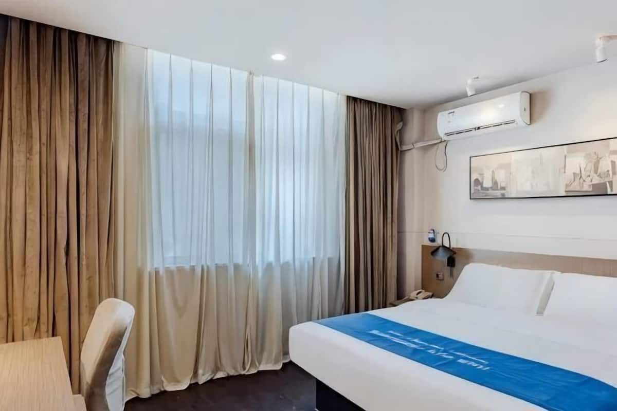 Quarto de hotel com cama, cadeira, escrivaninha, ar condicionado e janela com cortinas.