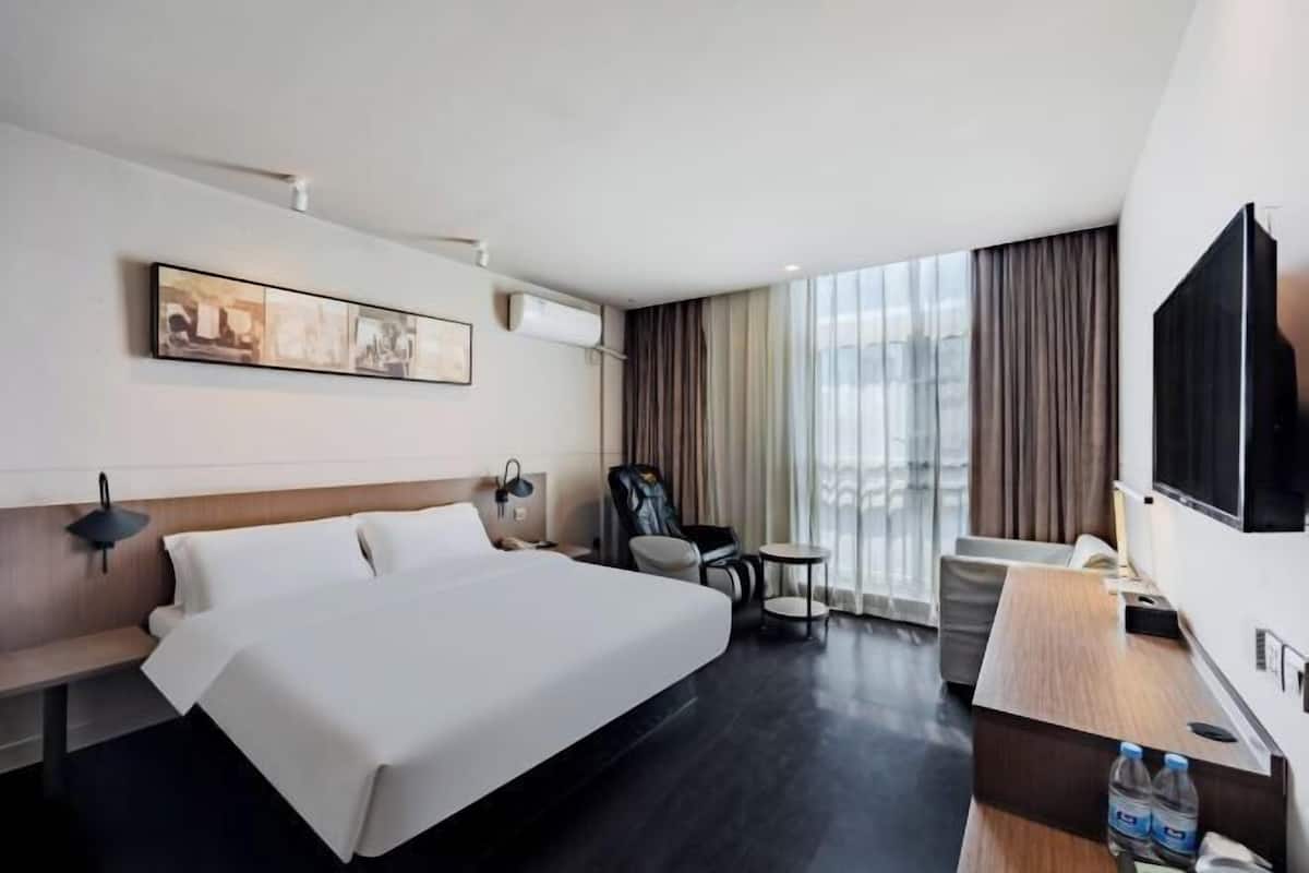 Quarto de hotel com cama, secretária, cadeira, televisão e janela com cortinas.