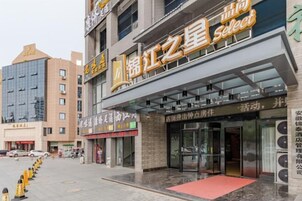 Entrada de hotel com tapete vermelho, portas de vidro e sinalização em língua estrangeira.