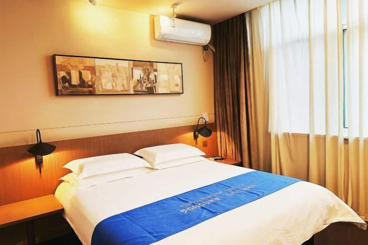 Quarto de hotel com cama, ar condicionado fixado na parede, quadro emoldurado e janela com cortinas.