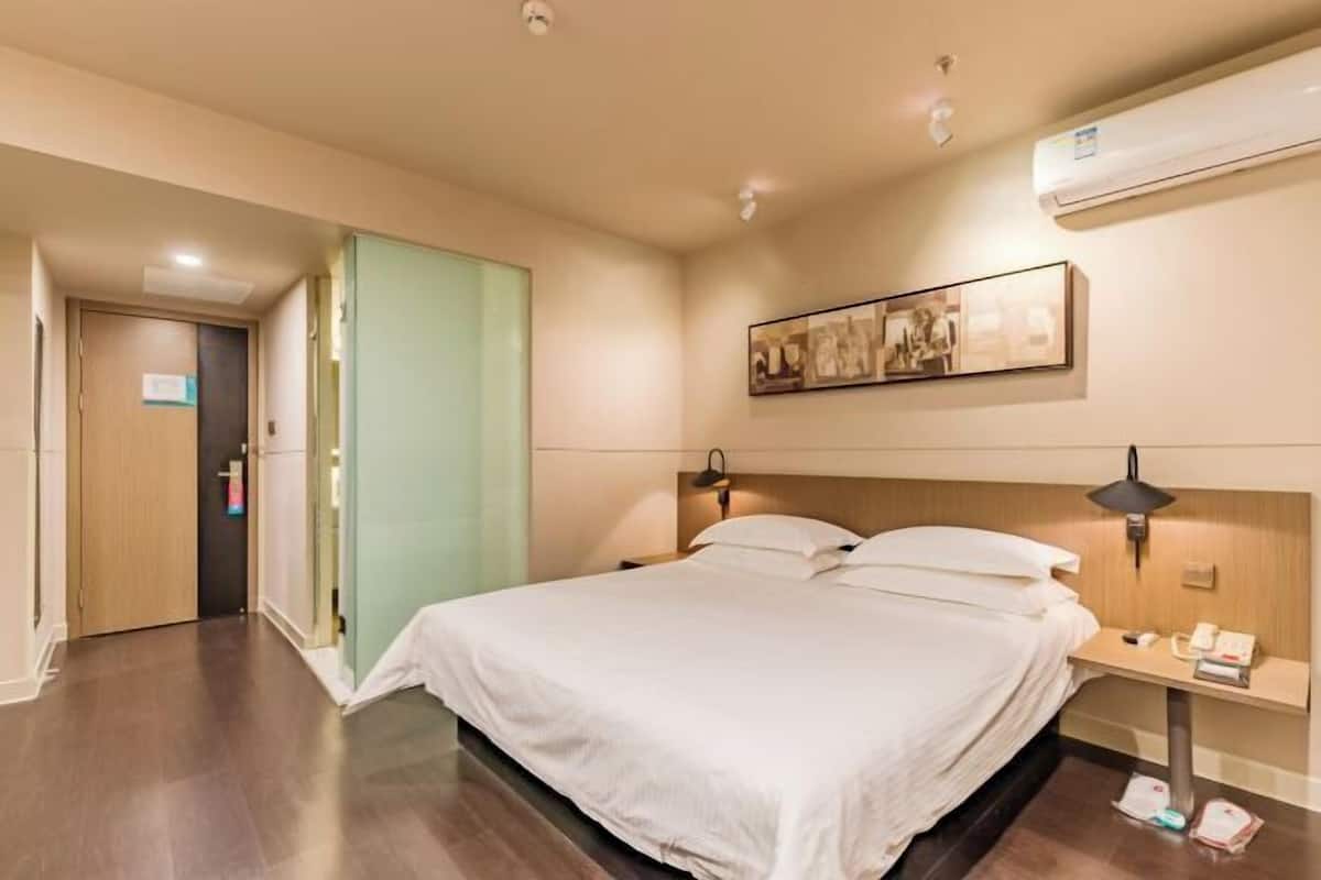 Quarto de hotel com cama, abajures, ar-condicionado fixado na parede e porta que dá acesso a outro quarto.