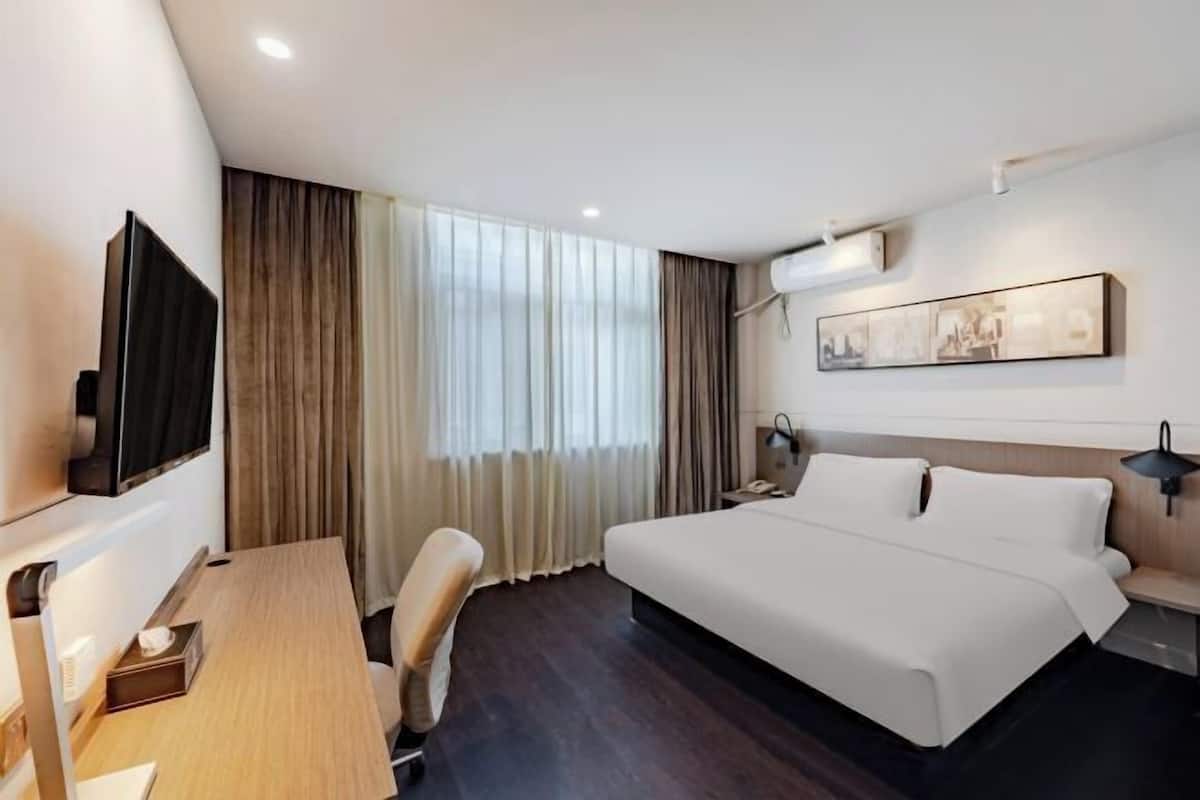 Quarto de hotel com cama, escrivaninha, cadeira, televisão de tela plana, mesa de cabeceira, abajur e janela com cortinas.