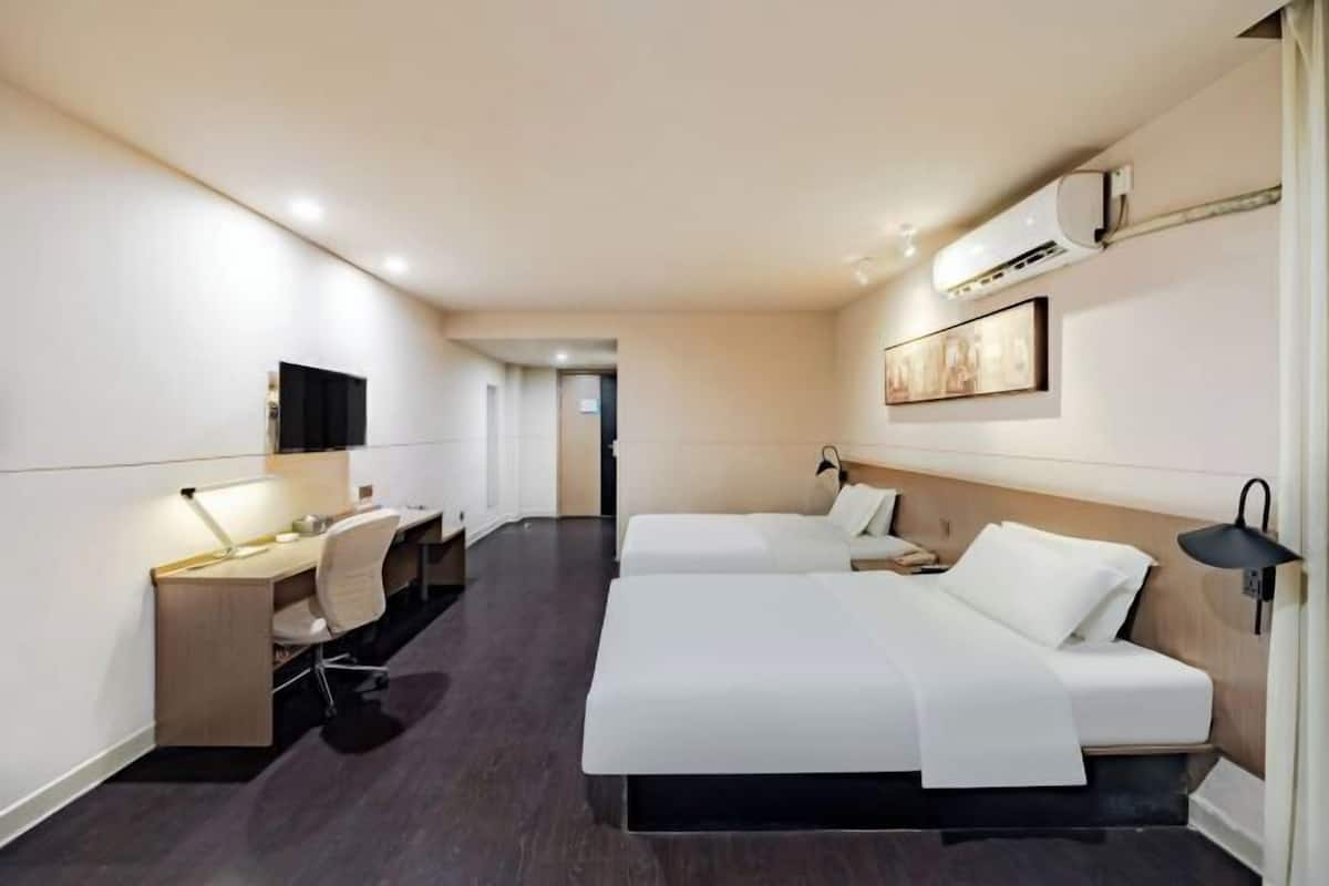 Quarto de hotel com escrivaninha, duas camas, televisão e ar condicionado.