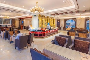Um saguão de hotel com área de bar central, espaços para sentar e um lustre.