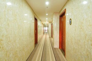 Corredor de hotel com paredes de mármore, portas de madeira e um tapete riscado.