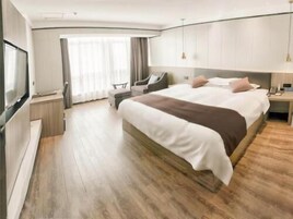 Quarto de hotel moderno com uma cama grande, televisão, escrivaninha e uma cadeira.
