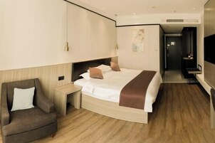 Quarto de hotel moderno com uma cama arredondada, um espaço de estar com uma poltrona, uma mesa de cabeceira e uma televisão.