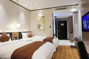 Quarto de hotel com duas camas, uma escrivaninha, uma televisão e um quadro na parede.