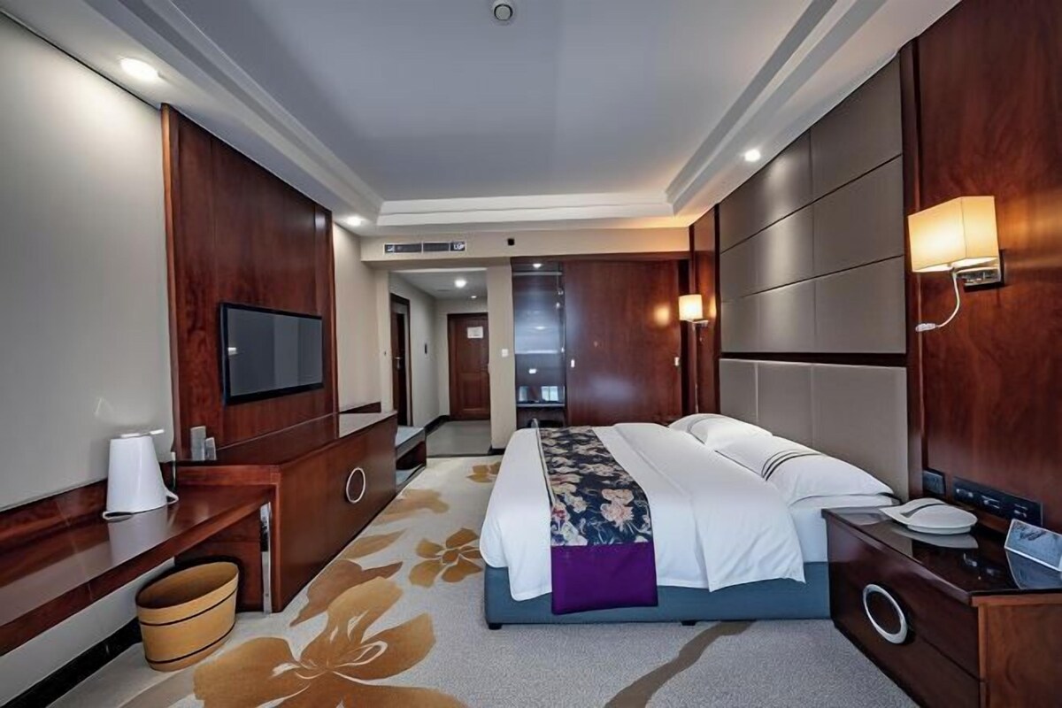 Quarto de hotel com cama, mesa de cabeceira, televisão e escrivaninha com cadeira.