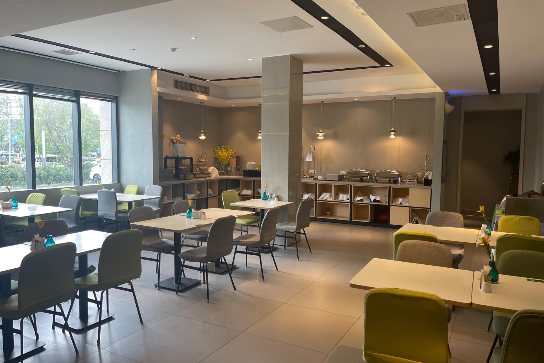 Uma área de refeições moderna com várias mesas e cadeiras, espaço de cozinha com eletrodomésticos e amplas janelas que proporcionam luz natural.