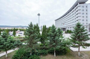 Um hotel moderno com fachada curva, cercado por um jardim bem cuidado e várias árvores.