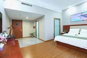 Quarto de hotel com piso de madeira, cama com roupa de cama branca, escrivaninha com cafeteira e um quadro na parede.