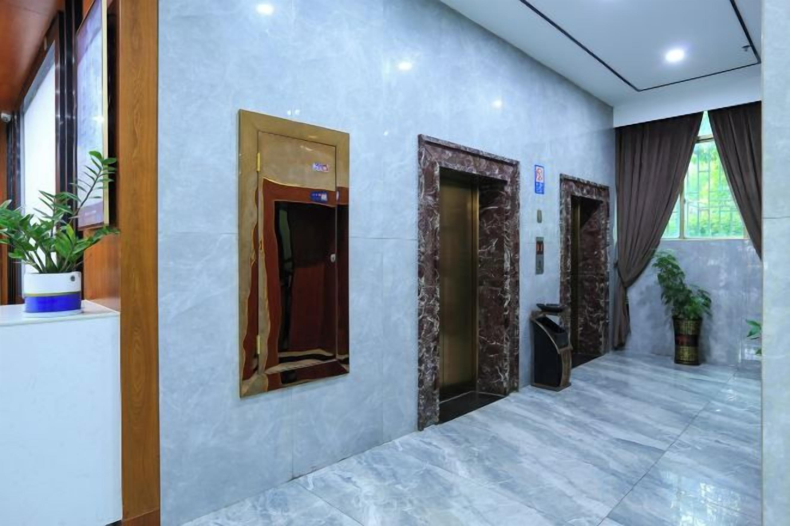Um hall de hotel com piso de mármore, balcão de recepção, uma planta e uma porta.