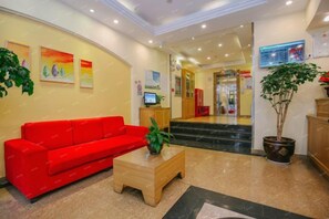Um saguão de hotel com um sofá vermelho, uma mesa de centro de madeira, uma planta em vaso e um balcão de recepção.
