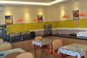 Interior de restaurante com mesas, cadeiras e balcão com alimentos expostos.