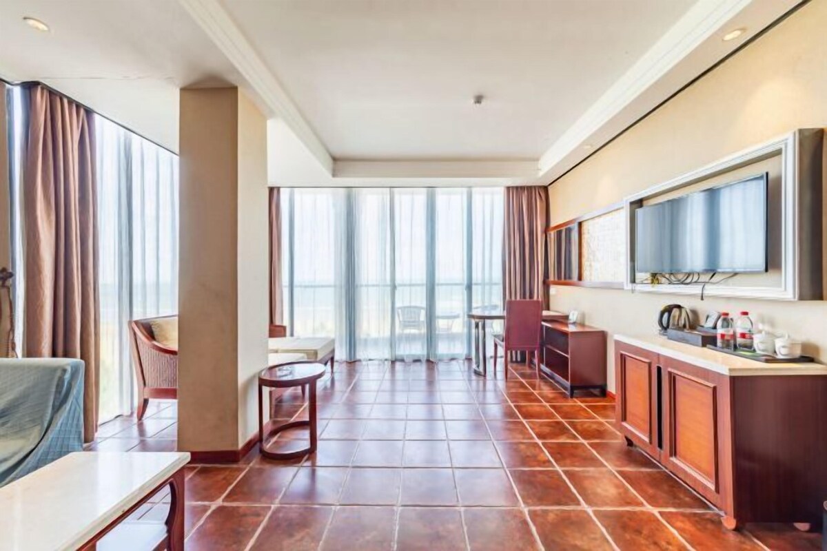 Quarto de hotel com uma janela grande, televisão de tela plana, uma mesa pequena, um sofá e um armário.