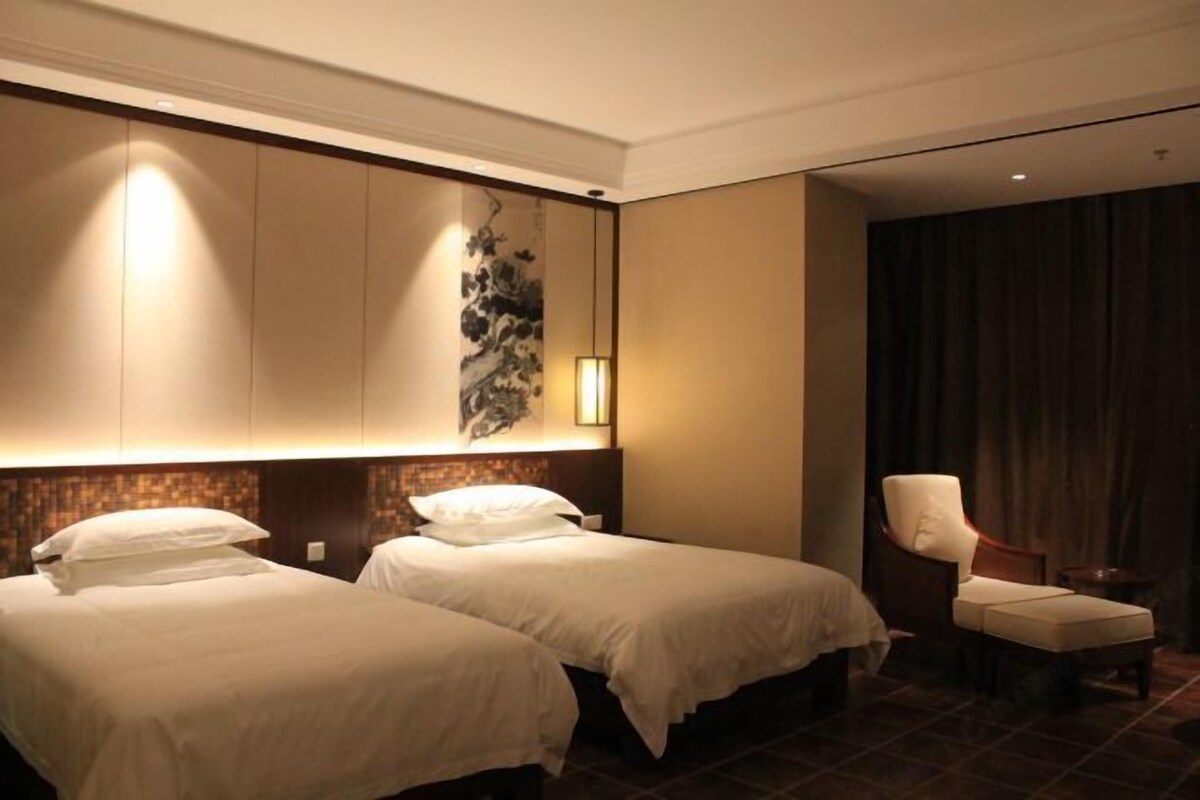 Quarto de hotel com duas camas, uma obra de arte grande na parede, uma cadeira e uma cortina.