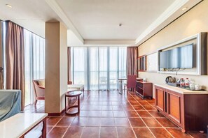 Quarto de hotel com uma janela grande, televisão de tela plana, mesa pequena e sofá.