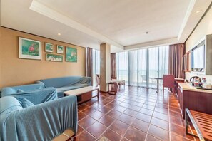 Quarto de hotel com cama, área de estar, mesa de jantar e uma janela grande.