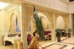 Um hall com estátua de pavão, arcos ornamentados e chão de mármore.