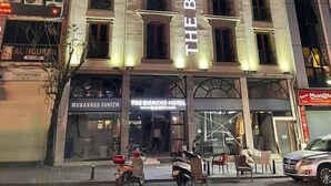 Um hotel com uma placa grande indicando "THE BIANCHO HOTEL" e uma loja na parte inferior com a inscrição "MUHANNED TURZIM" visível.