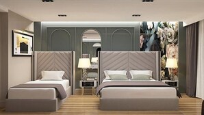 Quarto de hotel com duas camas, uma mesa de cabeceira com abajur, um espelho e uma parede decorada com flores.