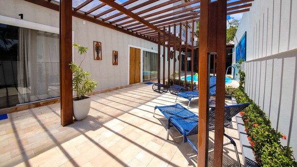 Uma área externa coberta com piscina, cadeiras de sol e plantas em vasos.