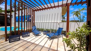 Uma área de estar coberta ao ar livre, com cadeiras e piscina ao fundo.
