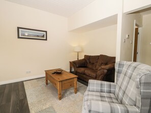 Uma sala de estar com um sofá de couro marrom, um sofá xadrez, uma mesa de centro de madeira e um quadro na parede.