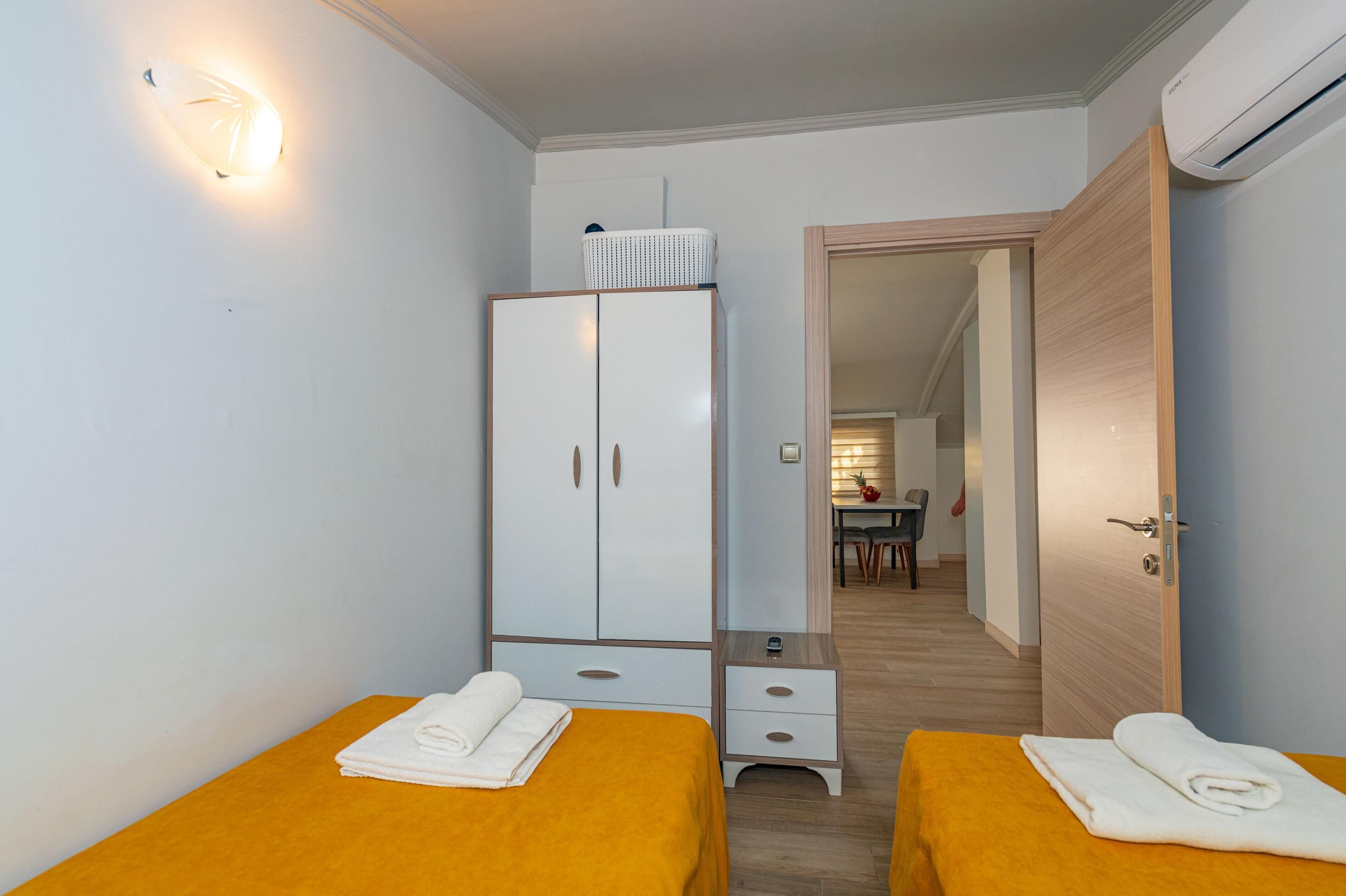 Quarto de hotel com duas camas, um guarda-roupa, uma mesa de cabeceira e um aparelho de ar condicionado.