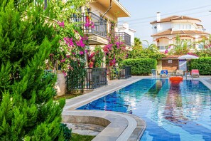 Piscina rodeada por vegetação exuberante e um edifício com várias andares e varandas.