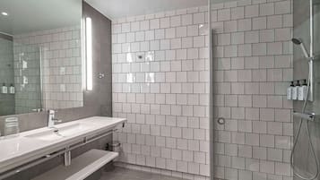 Um banheiro moderno com chuveiro em azulejo branco, um espelho grande e um banco.