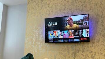 Uma TV de tela plana fixada em uma parede texturizada, exibindo a interface de um serviço de streaming com diversas opções de programas.
