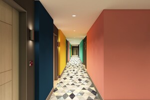 Um corredor vibrante e colorido com um chão de padrão geométrico, que leva a uma porta à esquerda.