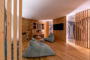 Quarto com paredes de madeira, televisão fixada na parede, armário com gavetas e um sofá.