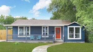 Uma casa pequena, térrea, com fachada azul escura, uma porta vermelha e um pequeno alpendre com cadeiras azuis.