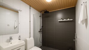 Uma casa de banho moderna com chuveiro, sanita, lavatório e espelho.