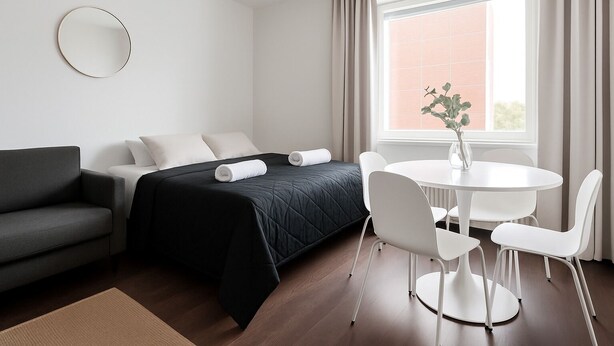 Quarto de hotel moderno com cama, sofá, mesa de jantar com cadeiras, espelho redondo e janela com cortinas.