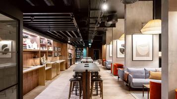 Um interior moderno com uma mesa de jantar comprida, banquetas de bar e área de estar com sofá e cadeiras.