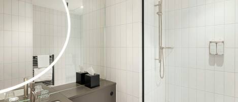 Uma casa de banho moderna com cabine de duche em vidro, toucador com lavatório e espelho com luz circular.
