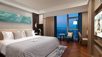 Quarto de hotel moderno com uma cama grande, vista para a cidade, uma mesinha e uma TV.