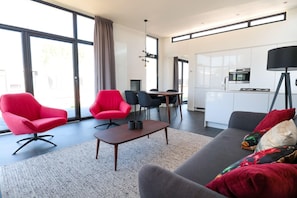 Uma sala de estar moderna com um sofá, cadeiras vermelhas, uma mesa de centro e um espaço de jantar com mesa e cadeiras.