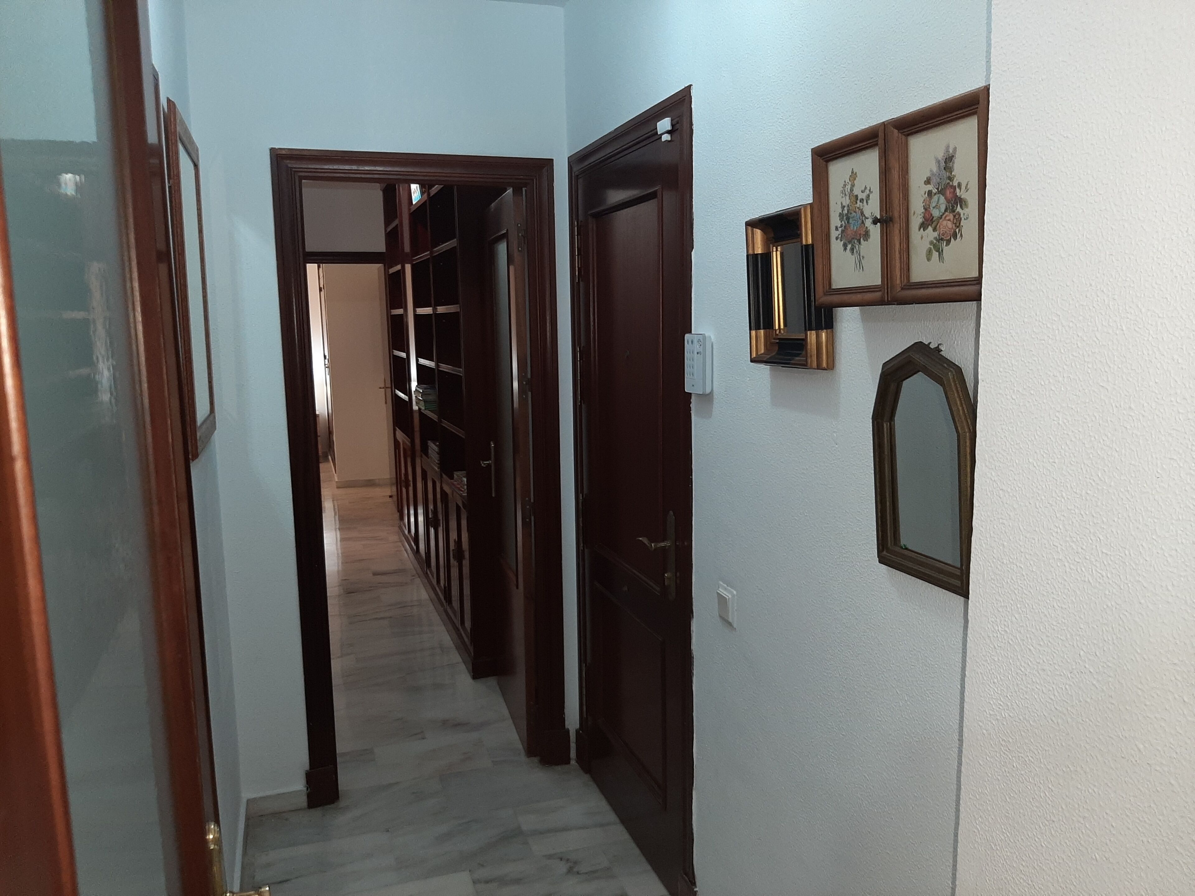 Um corredor com portas de madeira e parede branca decorada com quadros.