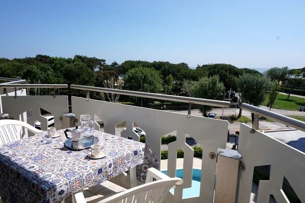 Varanda com mesa posta para dois, com vista para uma piscina e um parque.