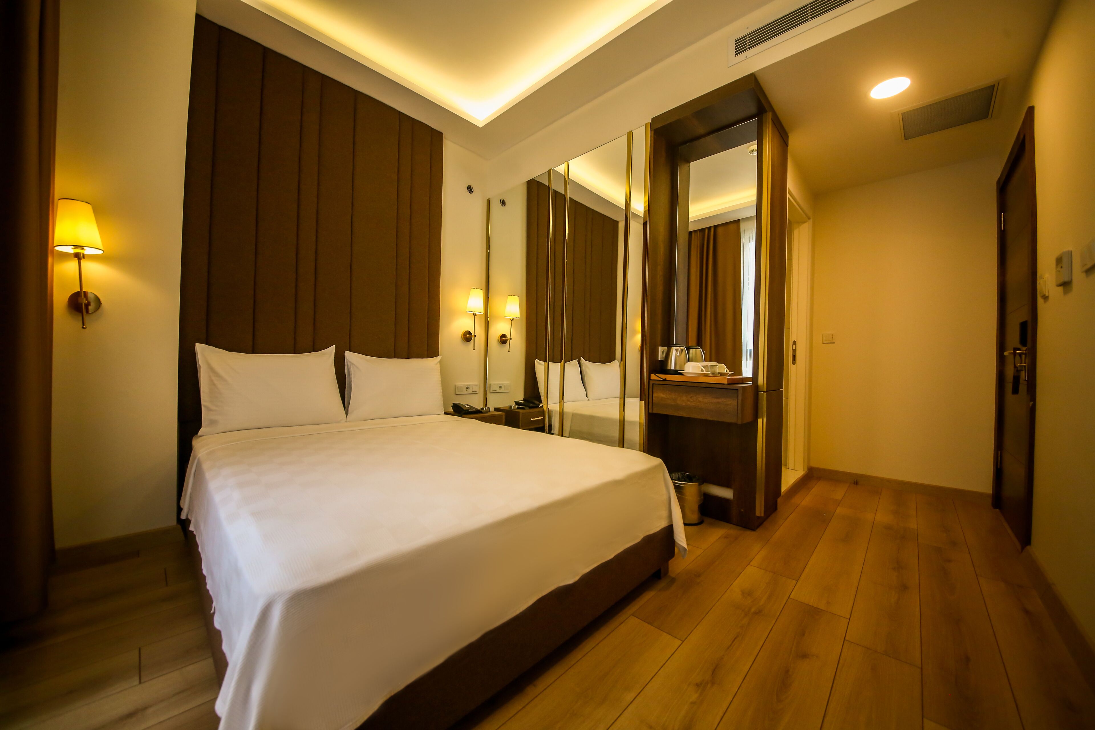 Quarto de hotel com cama grande, piso de madeira, espelho e um pequeno banheiro.