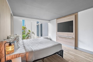Quarto moderno com cama, mesa de cabeceira, abajur e uma janela grande com vista.